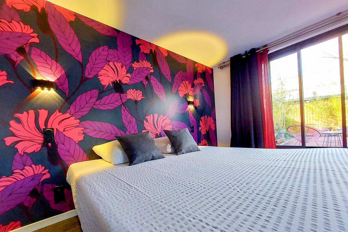 Quarto de hotel com uma cama grande, duas luzes fixadas na parede e vista para o exterior através de uma porta de correr.