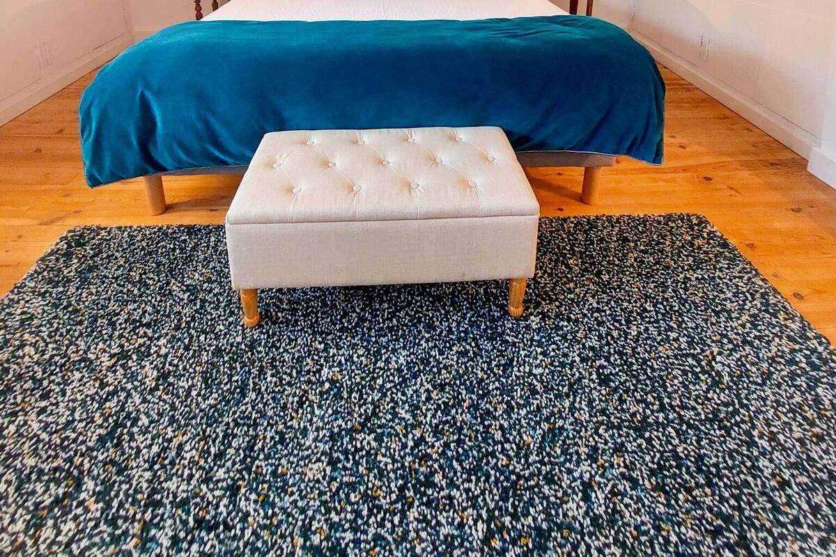 Quarto com cama, duas mesas de cabeceira, um banco, parede estampada e chão de madeira.