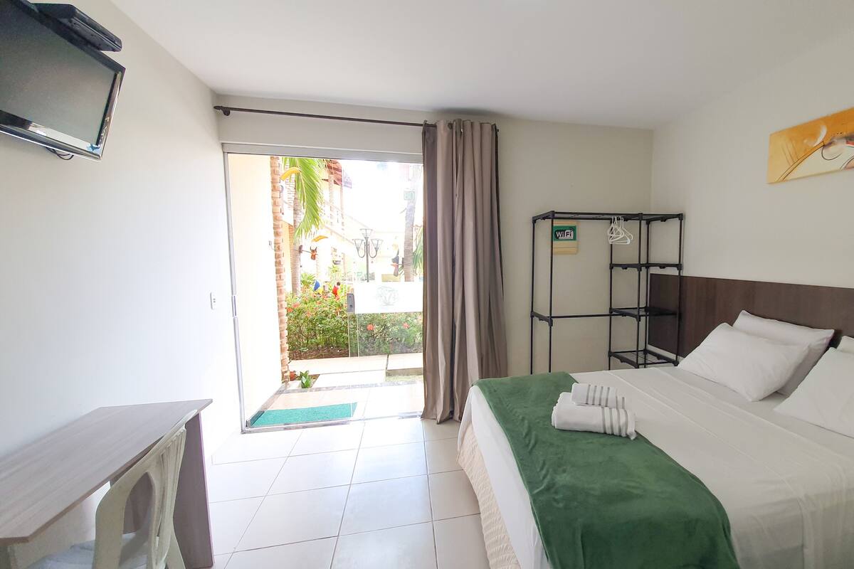 Quarto de hotel com cama, televisão, varanda e vista para o exterior, além de sinal de Wi-Fi.