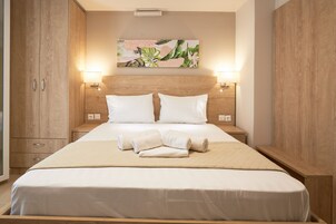 Cama bem arrumada com lençóis brancos e duas almofadas, com mesas de cabeceira de madeira com luminárias, num quarto com paredes de madeira e uma obra de arte com tema tropical acima da cama.