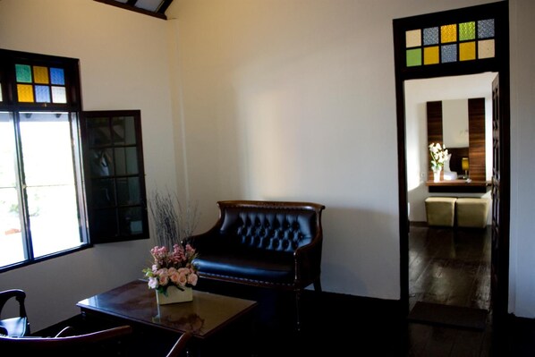 Quarto com sofá de couro escuro, mesa de madeira com um vaso de flores e janela com vitrais.