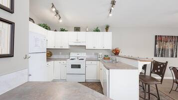 Cozinha moderna com armários brancos, fogão e pia. Há plantas na bancada e um quadro na parede.