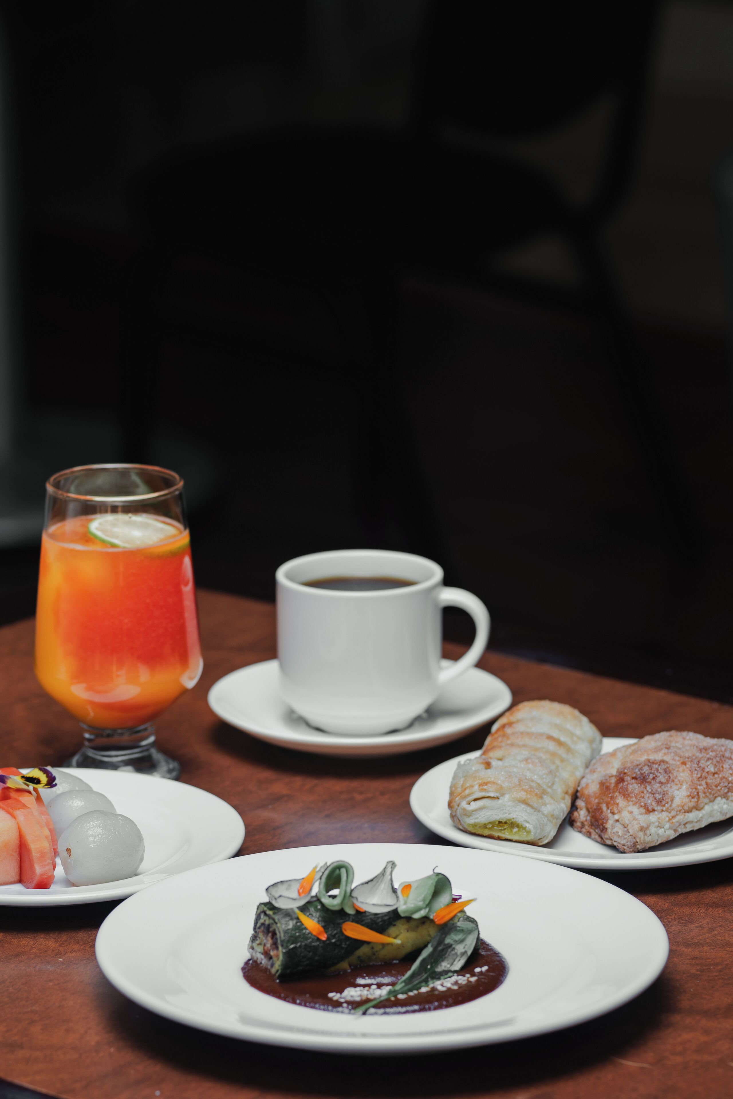 Uma mesa com um copo de suco de laranja, uma xícara de café e pratos de comida, incluindo um pastel enrolado e um prato de legumes.