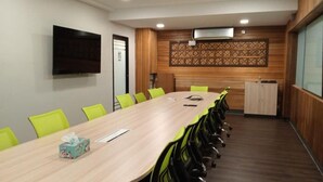 Uma sala de conferências com uma mesa comprida, cadeiras, uma televisão e um painel de parede estampado.
