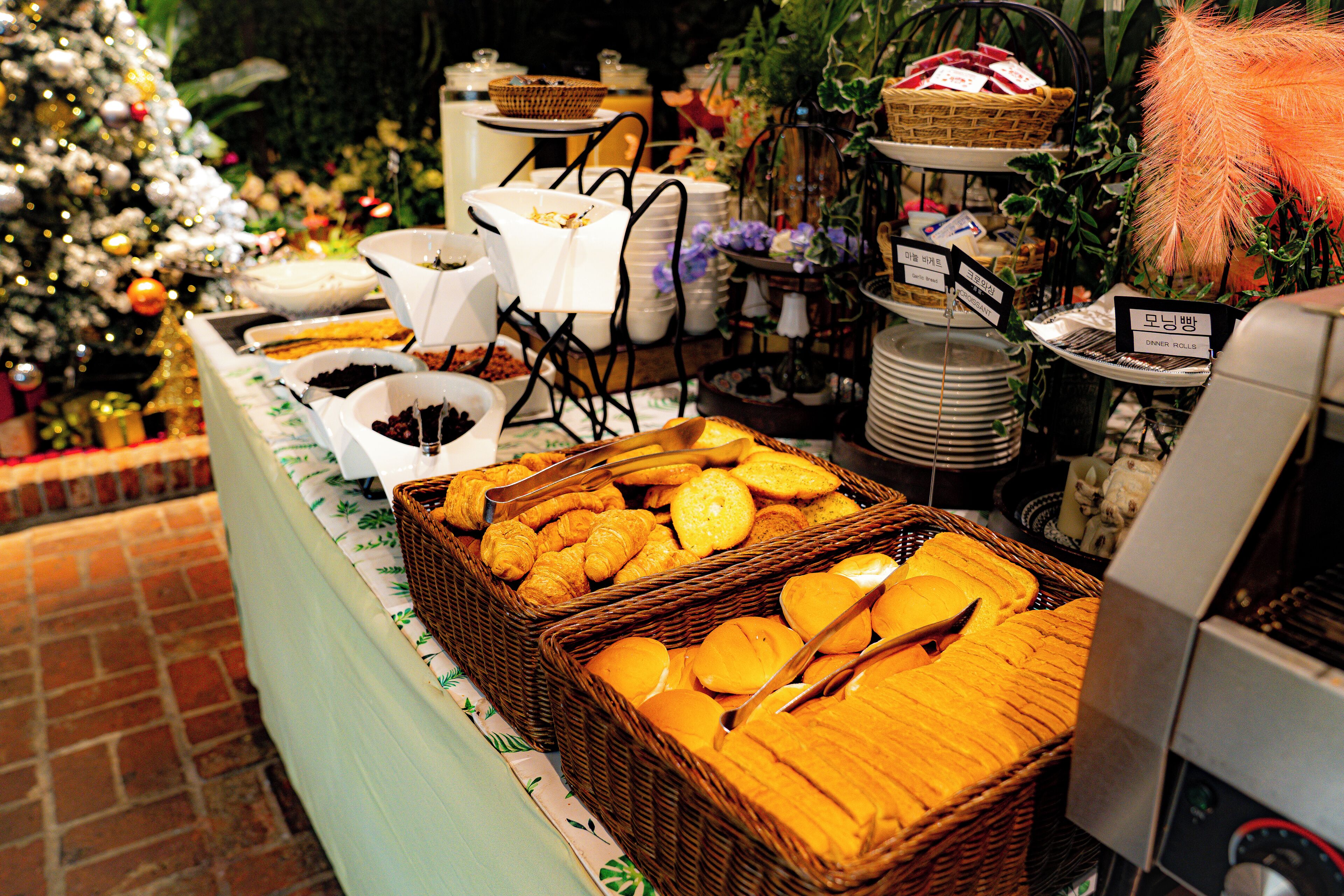 Uma mesa de buffet com diversos alimentos e uma árvore de Natal ao fundo.