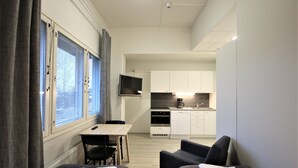 Quarto de hotel compacto com cama, escrivaninha, cadeira, televisão e cozinha compacta.
