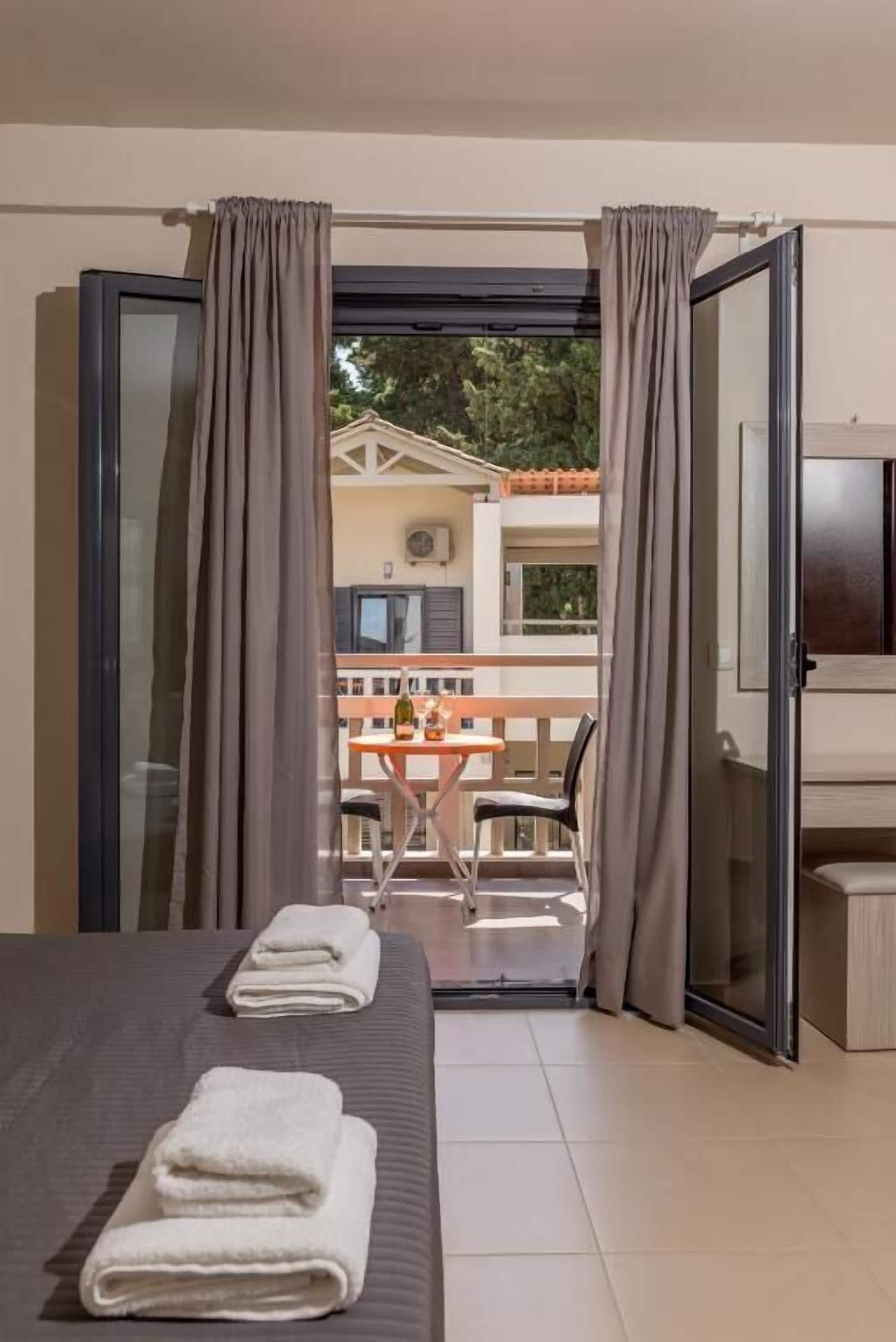Quarto de hotel com uma cama, televisão e varanda com mesa e cadeiras.