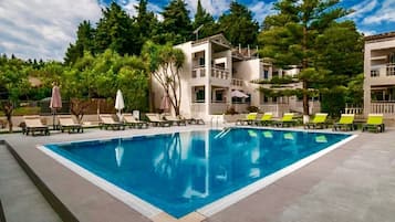 Piscina com espreguiçadeiras, rodeada por árvores e um edifício com varandas.