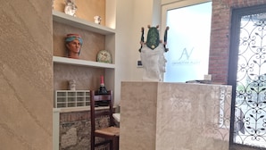 Uma área de recepção com balcão de mármore, uma cadeira de madeira e objetos decorativos em prateleiras.