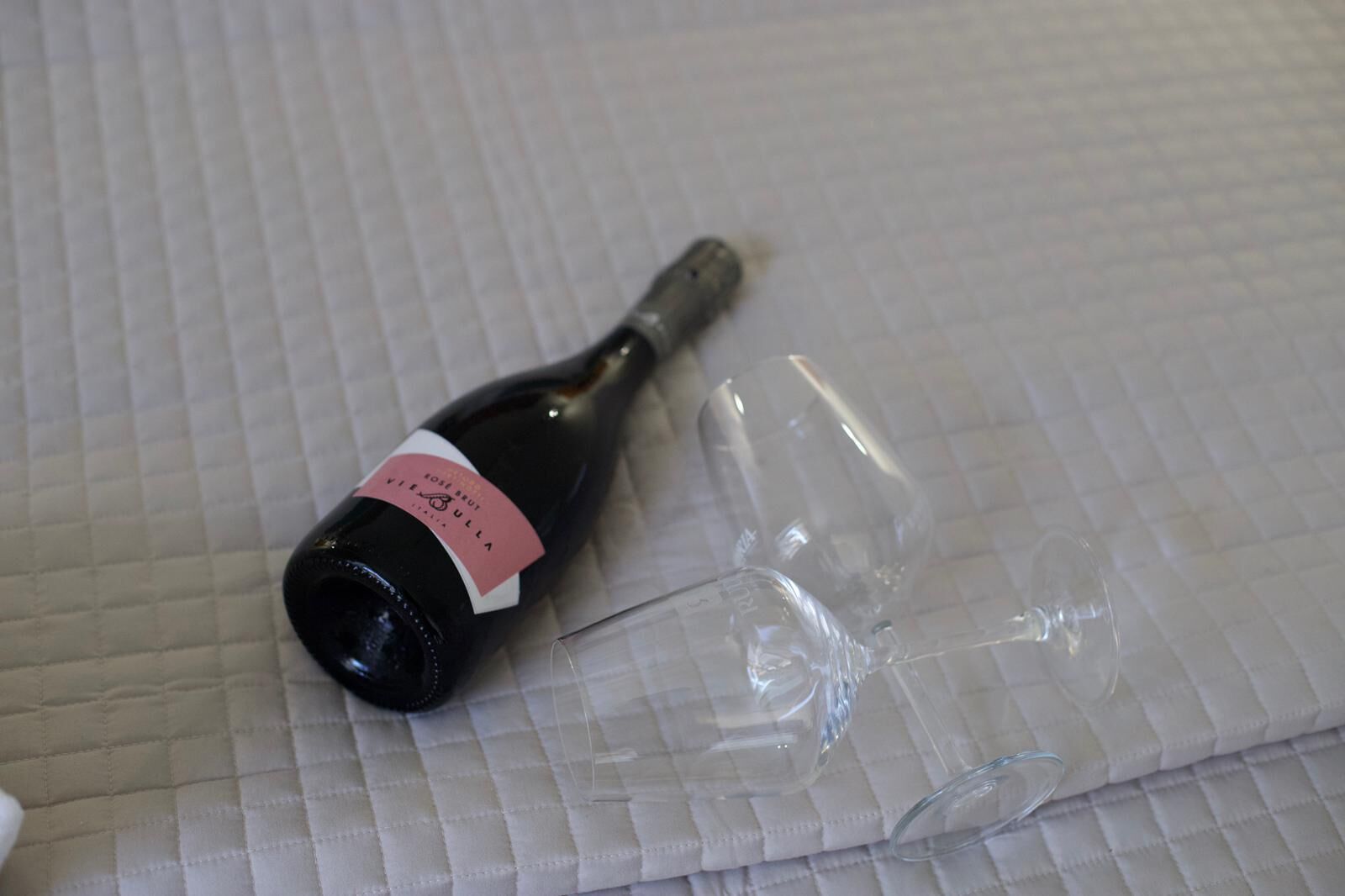 Uma garrafa de vinho e um copo sobre uma superfície acolchoada.