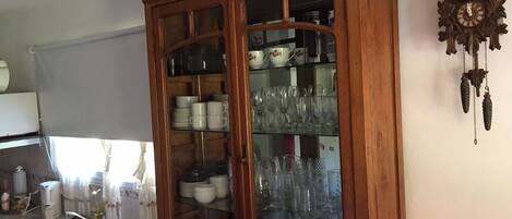 Uma cozinha com armário de madeira contendo pratos e copos, uma pia e um relógio fixado na parede.