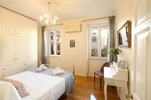 Quarto com cama, escrivaninha e cadeira. Possui janela com cortinas, lustre e ar condicionado na parede.