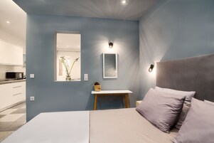 Quarto com cama, mesa de cabeceira e pequena escrivaninha com luminária.