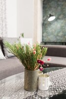 Uma mesa com um jogo americano trançado, um vaso com flores e uma caneca decorativa.