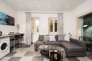 Uma sala de estar moderna com um sofá cinzento, uma mesa de centro de vidro e uma máquina de lavar.