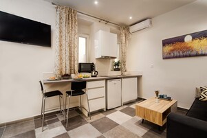 Cozinha compacta com área de refeições, uma TV de tela plana na parede e um quadro sobre o sofá.