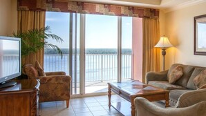 Quarto de hotel com varanda, sofá, televisão e duas luminárias.