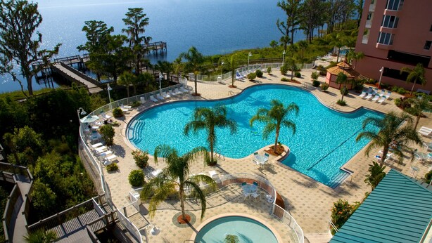 Uma piscina grande e sinuosa com espreguiçadeiras e palmeiras, rodeada por um deck e vista para a água.
