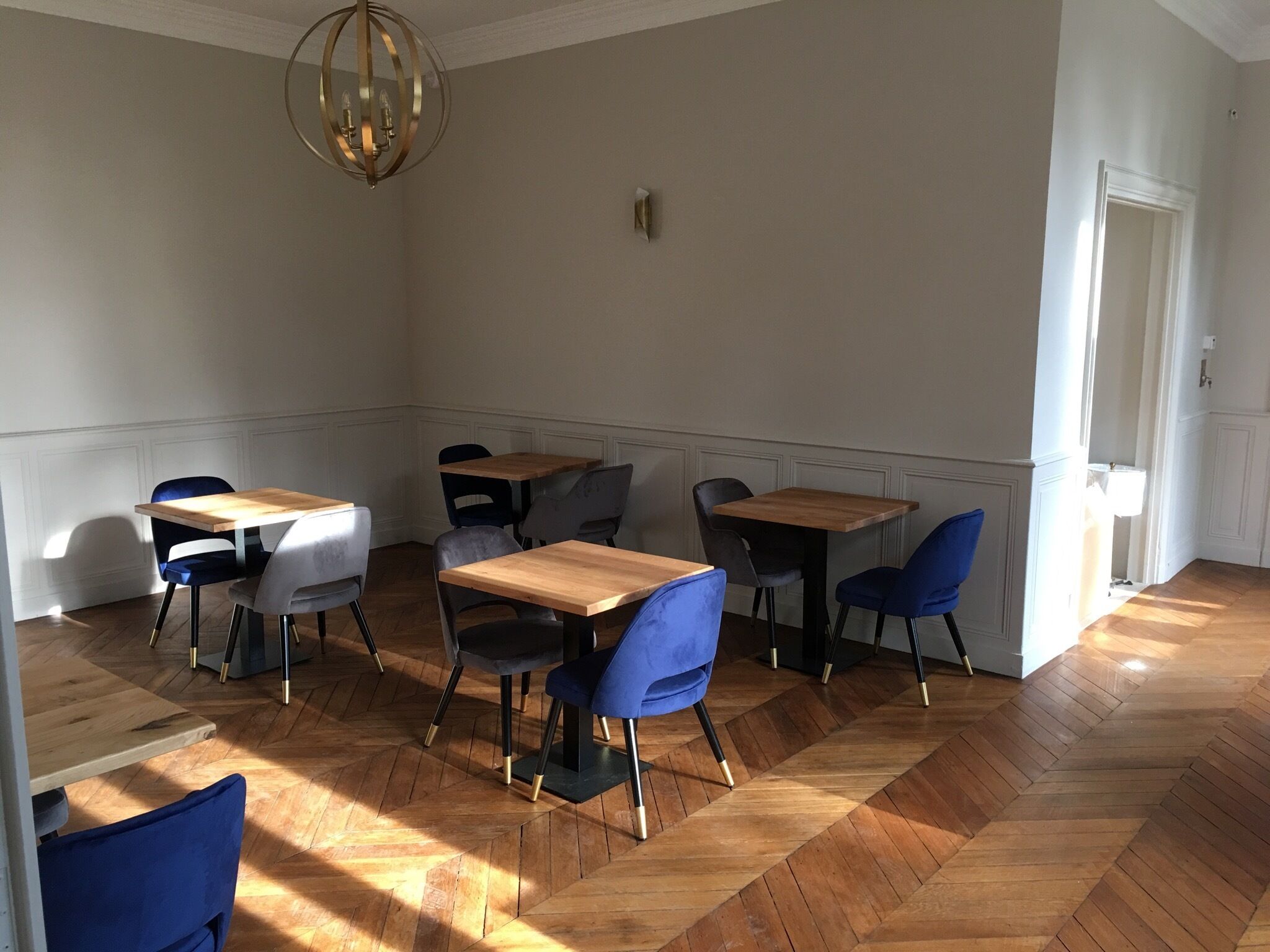 Uma sala de jantar com mesas de madeira e cadeiras azuis, um candelabro e um padrão de piso em herringbone.