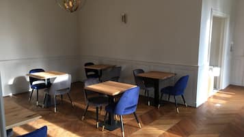 Uma sala de jantar com mesas de madeira e cadeiras azuis, um candelabro e um padrão de piso em herringbone.