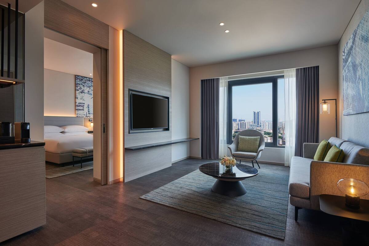 Quarto de hotel moderno com uma grande janela, televisão de tela plana, sofá, mesa de centro e cama.