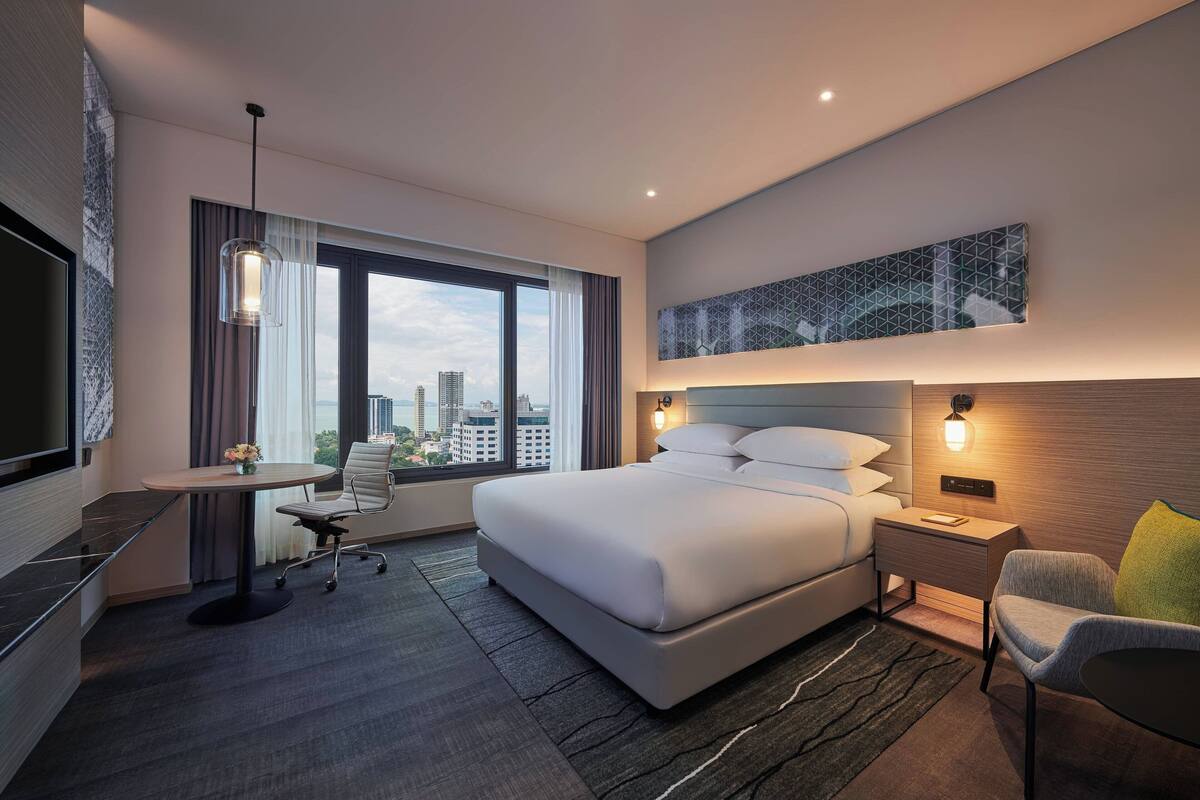 Quarto de hotel moderno com uma cama grande, uma mesa, uma cadeira e uma televisão.