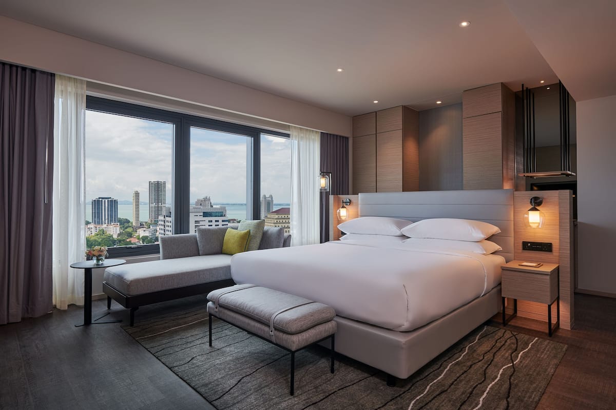 Quarto de hotel moderno com uma cama grande, área de estar, uma pequena mesa e vista para a cidade.
