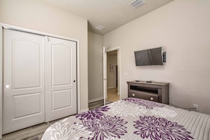Quarto com cama, guarda-roupa, televisão na parede e porta para outro cômodo.