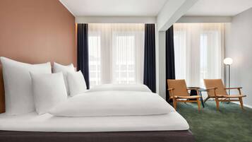 Quarto de hotel com uma cama grande, duas cadeiras, uma mesinha e um abajur.