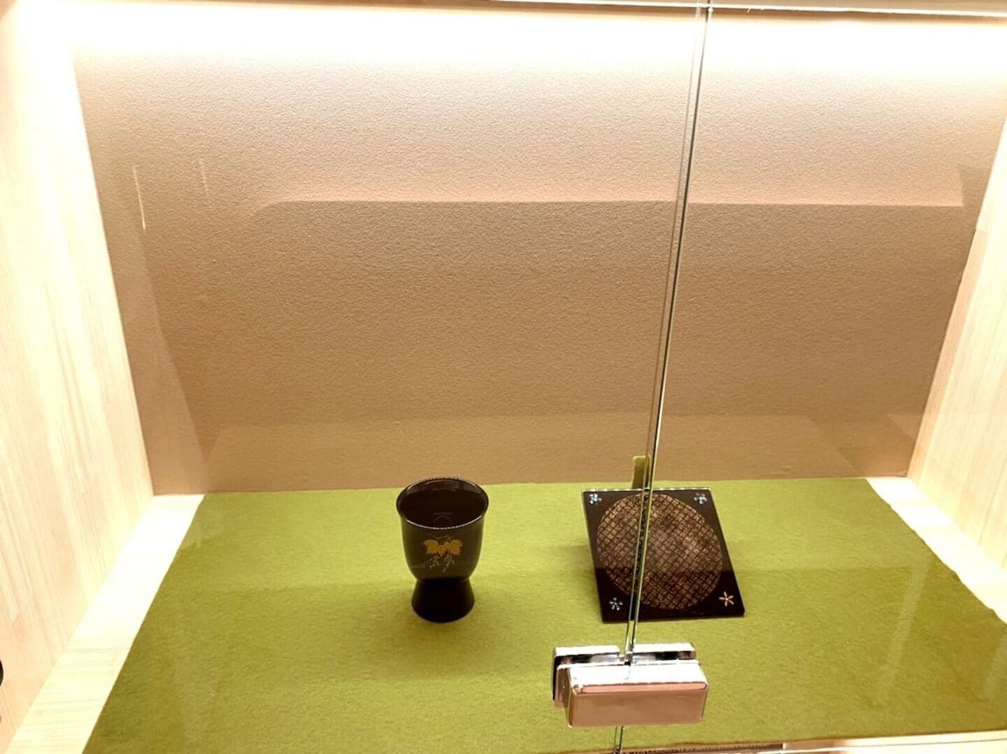 Quarto com carpete verde, luminária pendente e pequena mesa com objeto decorativo.