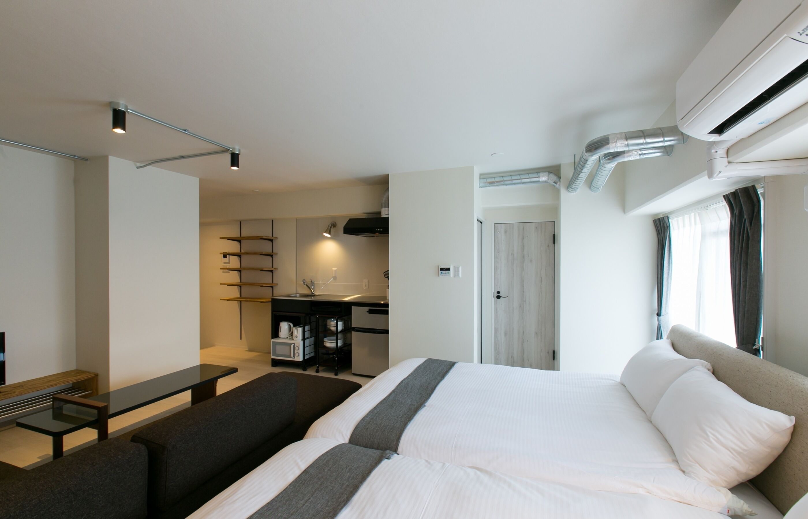 Quarto de hotel moderno com uma cama grande, uma escrivaninha e uma cozinha compacta.