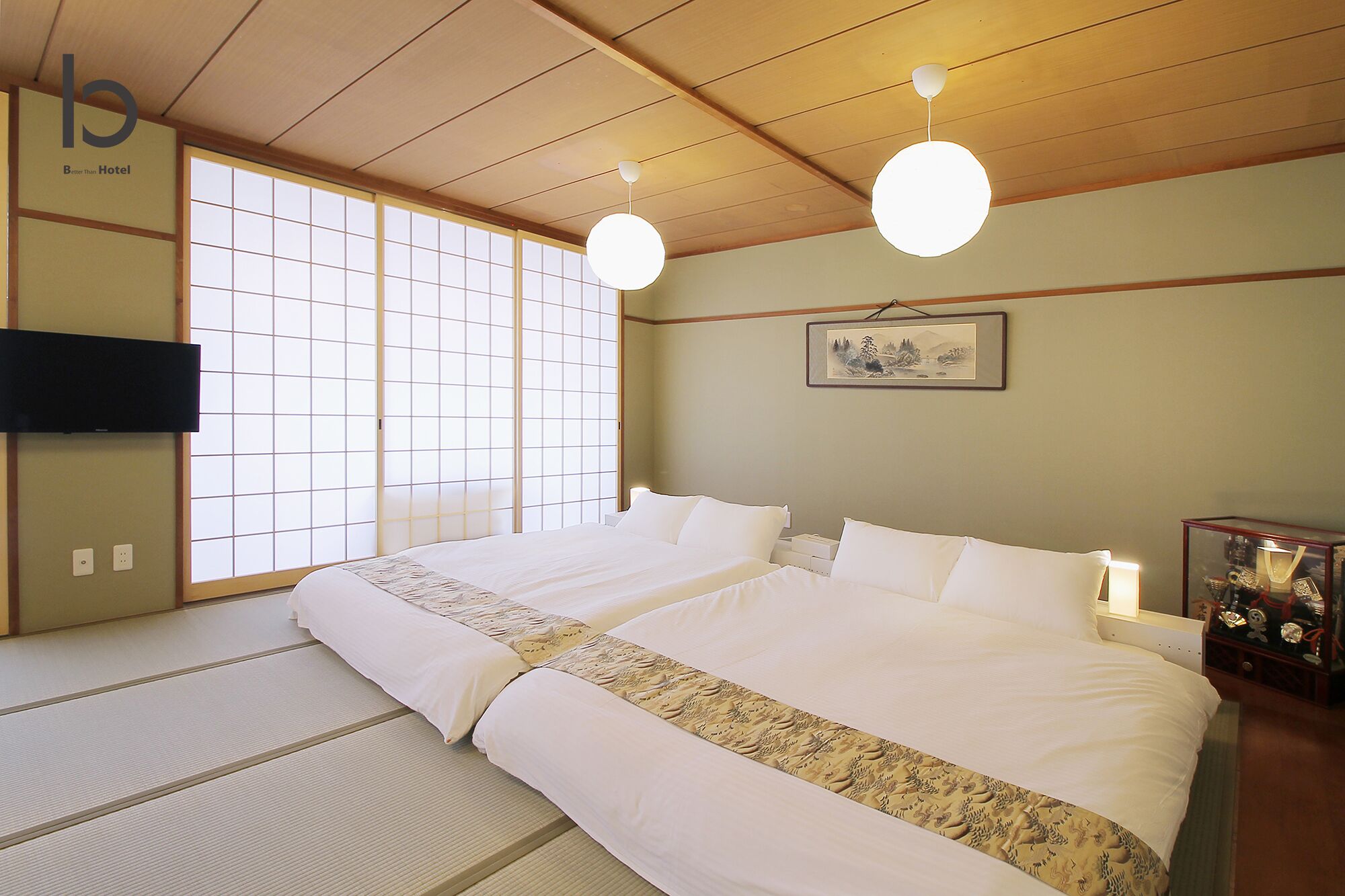 Quarto de hotel japonês tradicional, com piso de tatame, uma cama grande com roupa de cama branca, uma televisão na parede e um painel shoji.