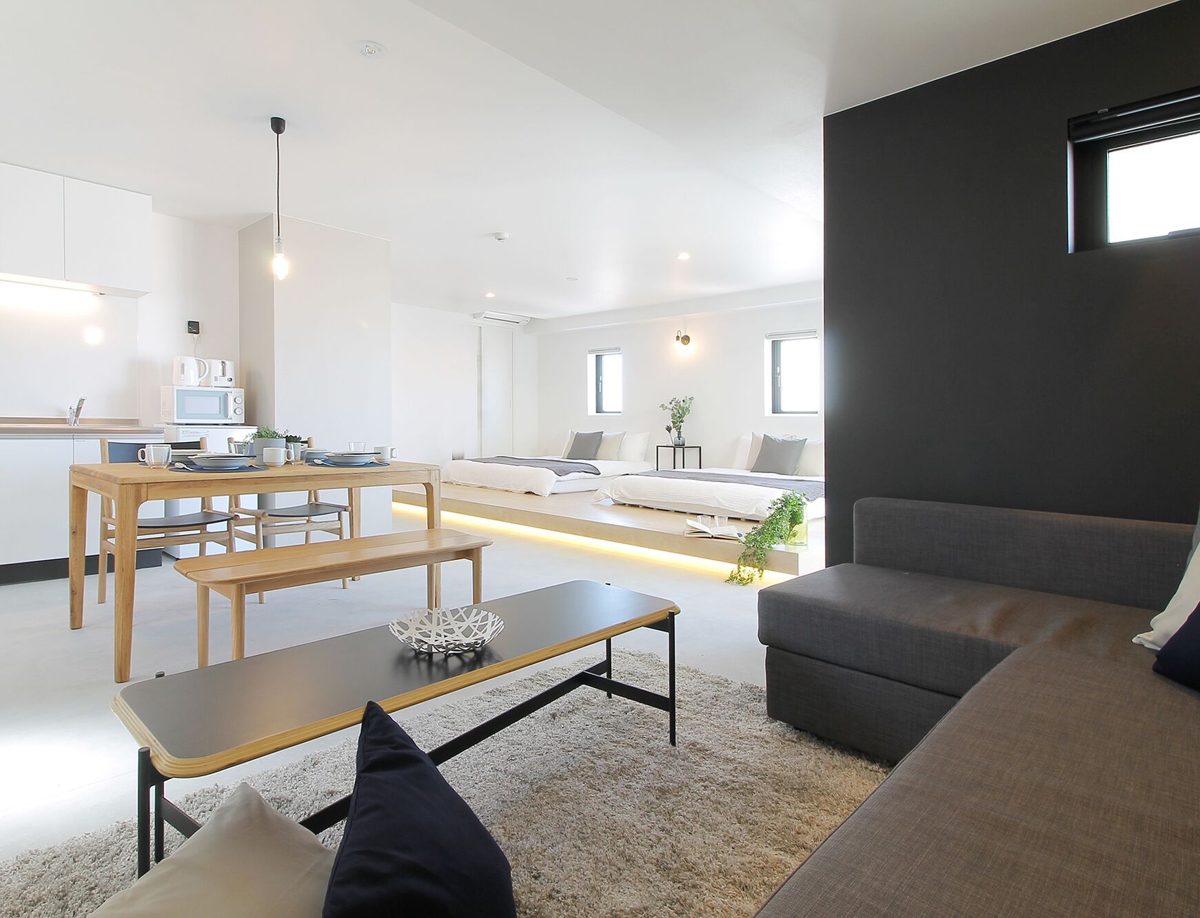 Uma sala de estar moderna com um sofá, uma mesa de jantar e uma área de cozinha ao fundo.