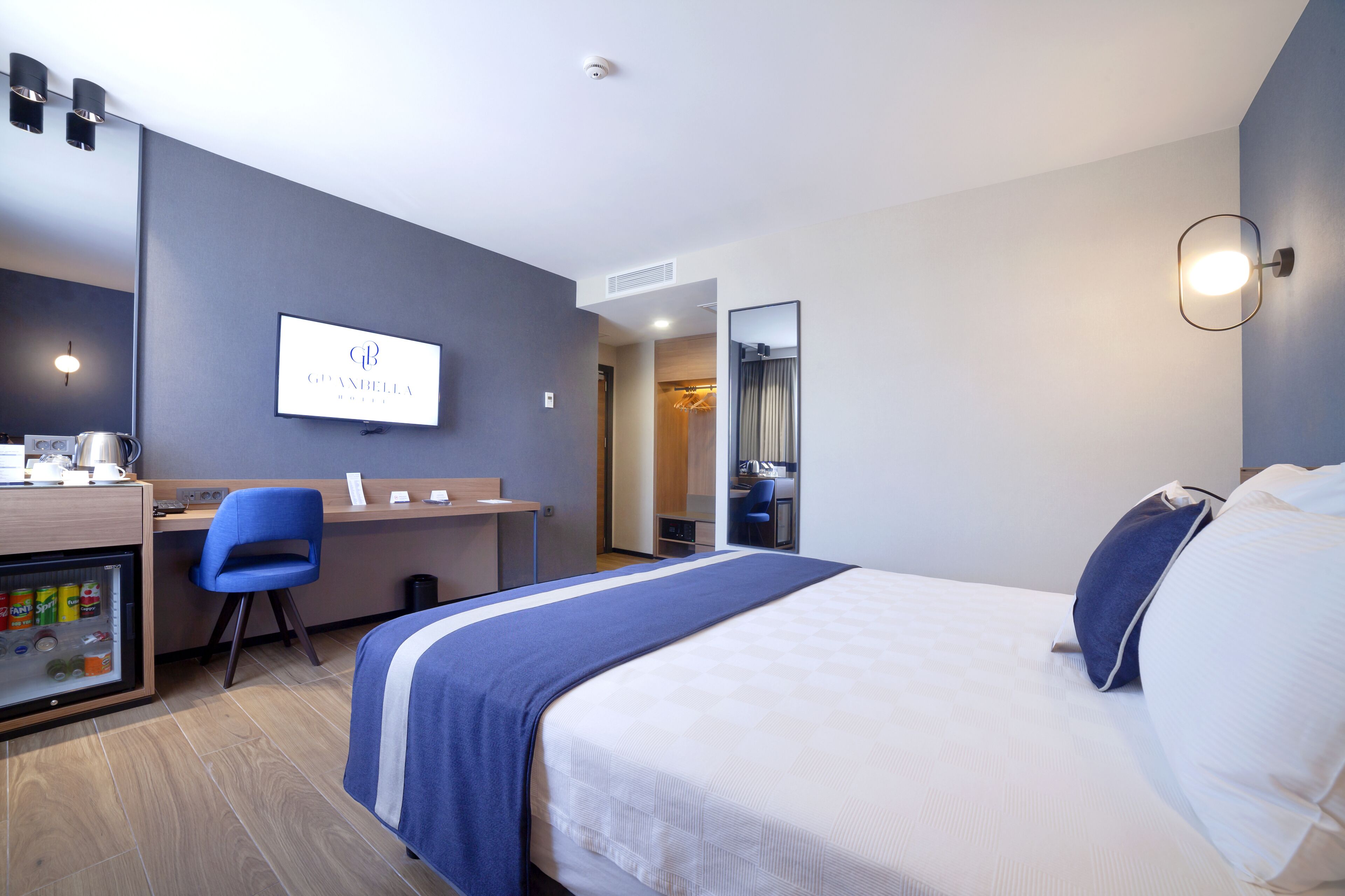 Quarto de hotel com cama, escrivaninha, cadeira, televisão e frigorífico.