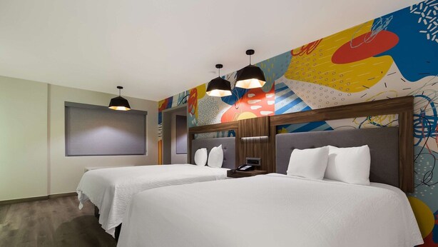 Quarto de hotel com duas camas, um grande mural abstrato na parede e luminárias pendentes.