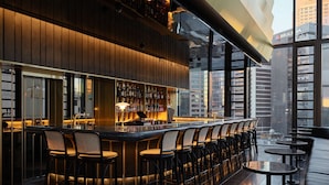 Um bar moderno com um balcão comprido, vários bancos altos e uma área de estar com mesas redondas.