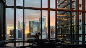 Um saguão de hotel moderno com grandes janelas que oferecem vista do horizonte urbano ao pôr do sol.