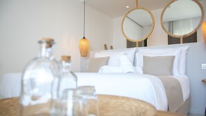 Cama bem arrumada com lençóis brancos, um espelho redondo e uma luminária pendente em um quarto de hotel moderno.