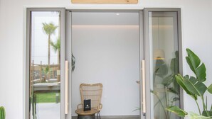 Uma área de recepção com uma placa sobre a porta, uma cadeira de vime e um vaso de planta.
