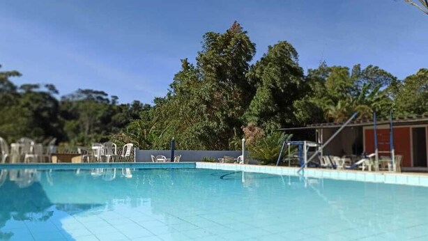 Uma piscina com água azul cristalina, cercada por árvores e um edifício com fachada vermelha.