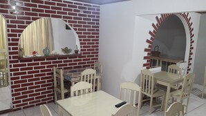 Uma área de refeições com parede de tijolos, um espelho redondo e uma mesa branca com cadeiras.