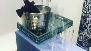 Uma área de bar com um balde de metal contendo uma garrafa, um guardanapo preto e vários copos de vidro transparentes sobre uma bandeja azul.