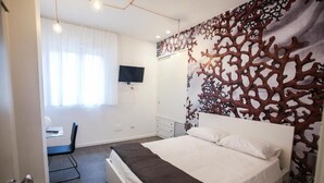 Quarto de hotel moderno com uma cama grande, uma escrivaninha e uma televisão fixada na parede.