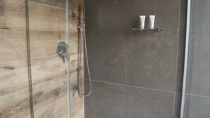 Um chuveiro moderno com porta de vidro, parede de madeira e parede revestida de azulejos cinzas.