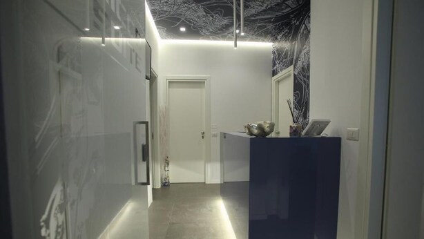 Um corredor moderno com uma parede azul escura de destaque, uma porta branca e uma pequena tigela decorativa numa prateleira.
