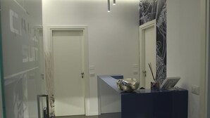 Uma área de recepção moderna com divisória de vidro, balcão de atendimento, porta e parede com desenhos abstratos.