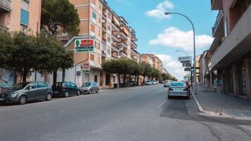 Vista da rua com edifícios altos, carros estacionados e céu claro.