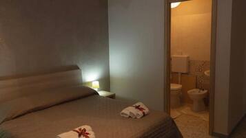Quarto de hotel com cama, mesa de cabeceira e banheiro com vaso sanitário e bidê.