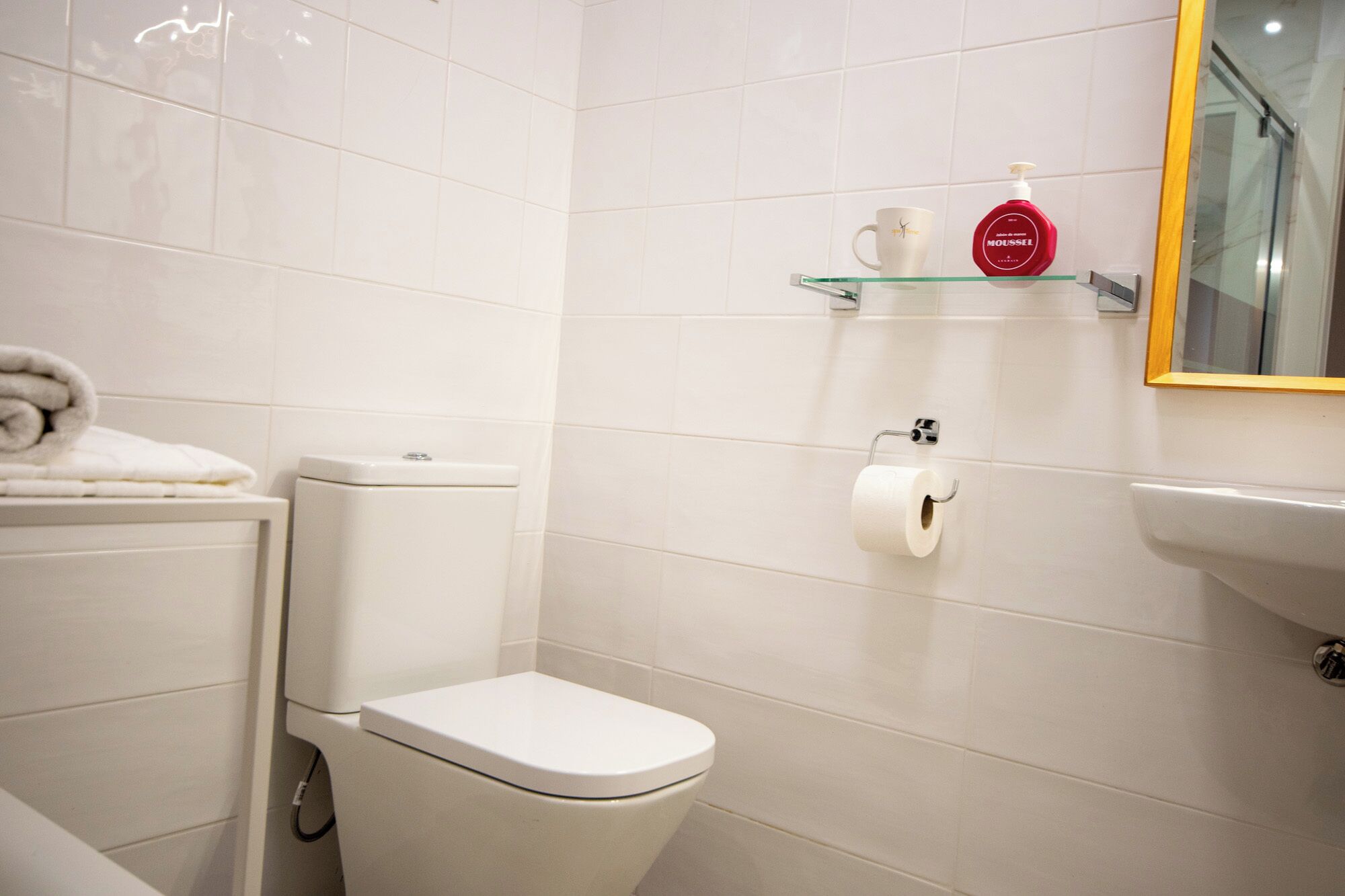 Uma casa de banho moderna com sanita, uma prateleira de vidro com artigos de higiene pessoal e um espelho.