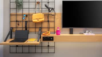 Um espaço de trabalho com um laptop, uma TV e um painel de grade com diversos objetos, como um boné, óculos de sol, uma bolsa e uma câmera.